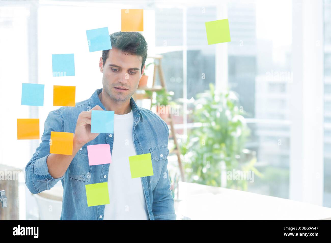 Man wearing denim shirt placing blue sticky note on glass partition in ...