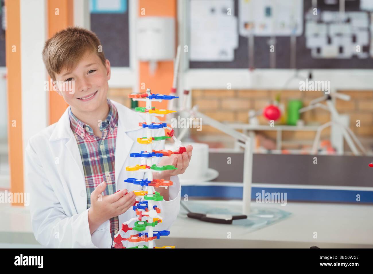 Smiling boy holding plastic DNA double helix model at lab bench wearing ...