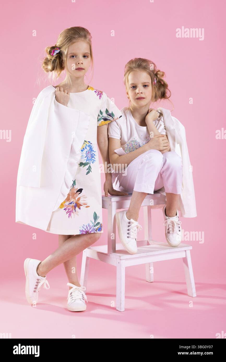 Portrait of twin girls on a powder background. One girl in a dress is ...