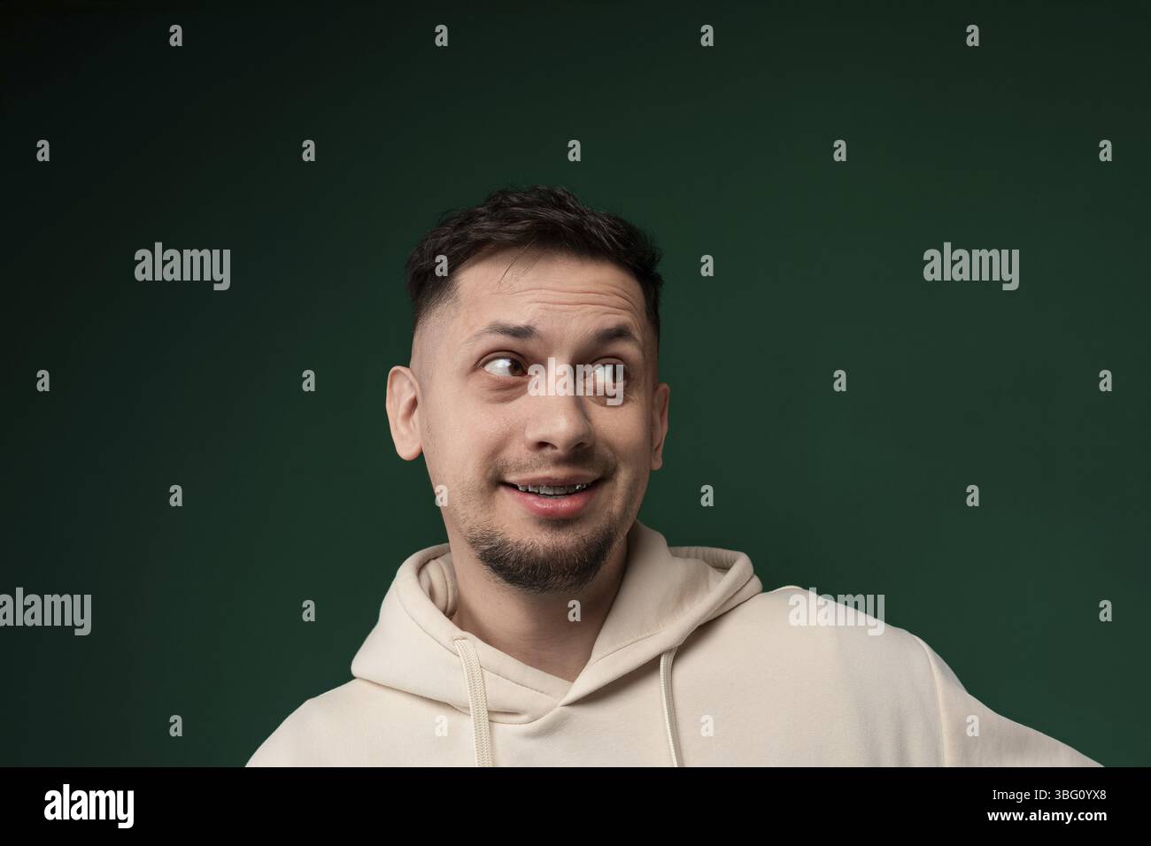 A man wearing a hoodie is pulling a funny face, contorting his features ...