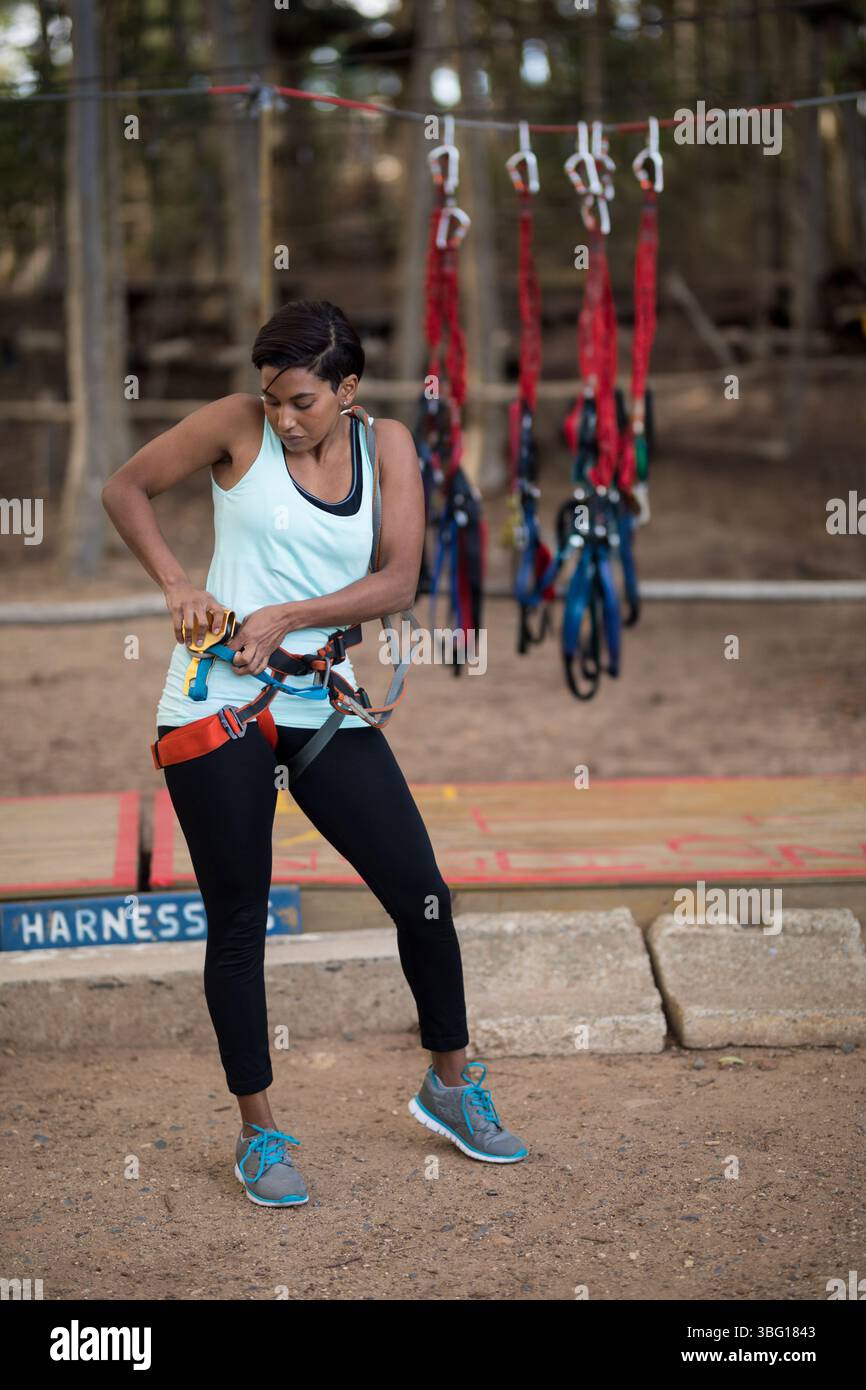 Woman fastening safety harness with carabiners around waist on wooden ...