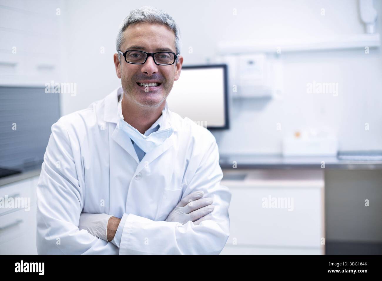 Middle-aged man standing with arms crossed in exam room wearing lab ...