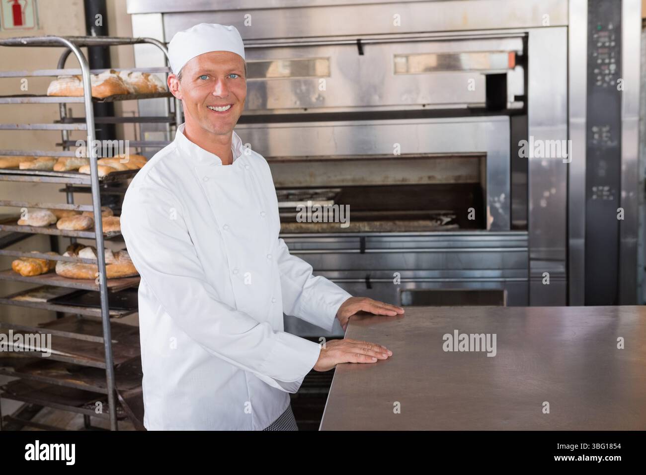 Mature male baker arranging bread loaves on metal rack near stainless ...