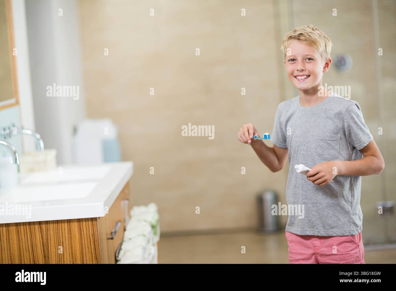 Boy child brushing teeth in home bathroom beside vanity with blue ...