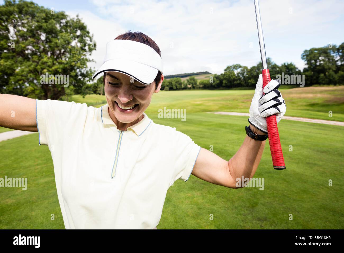 Senior woman raising arms holding red-grip golf club on fairway wearing ...