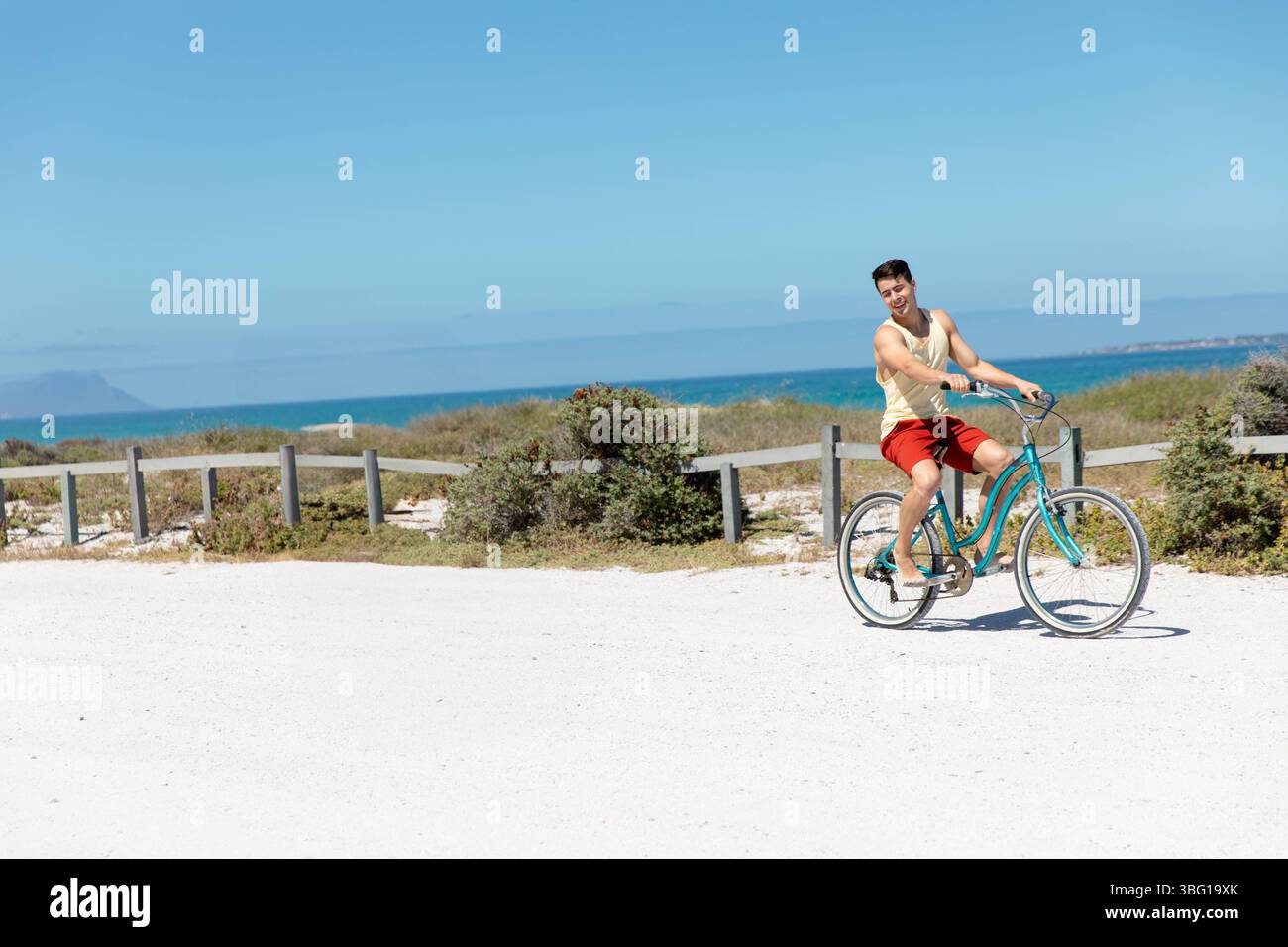 Cyclist is riding teal cruiser bicycle along sandy path near turquoise ...