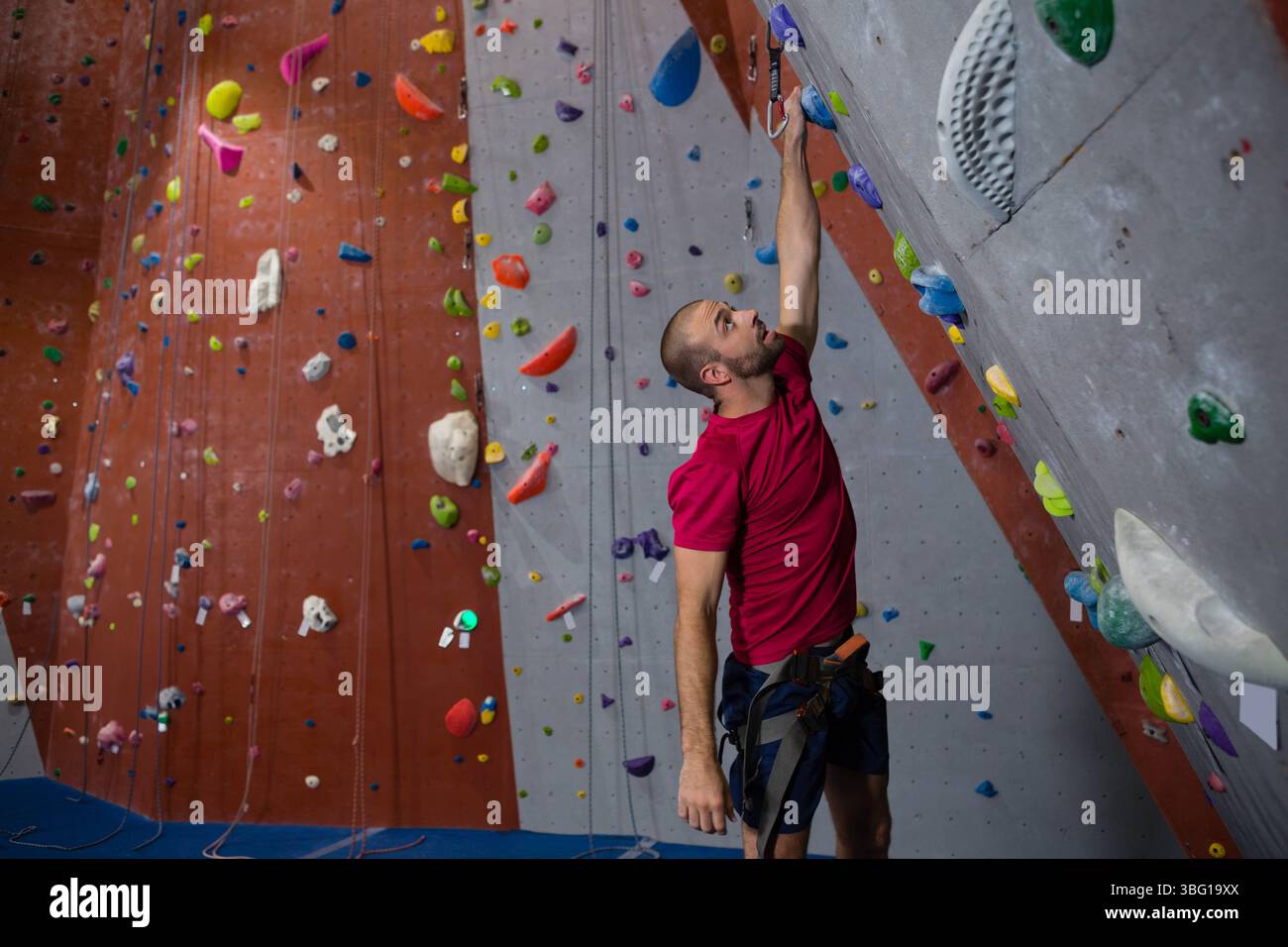 Climber scaling wall inside gym, using harness and rope with colorful ...
