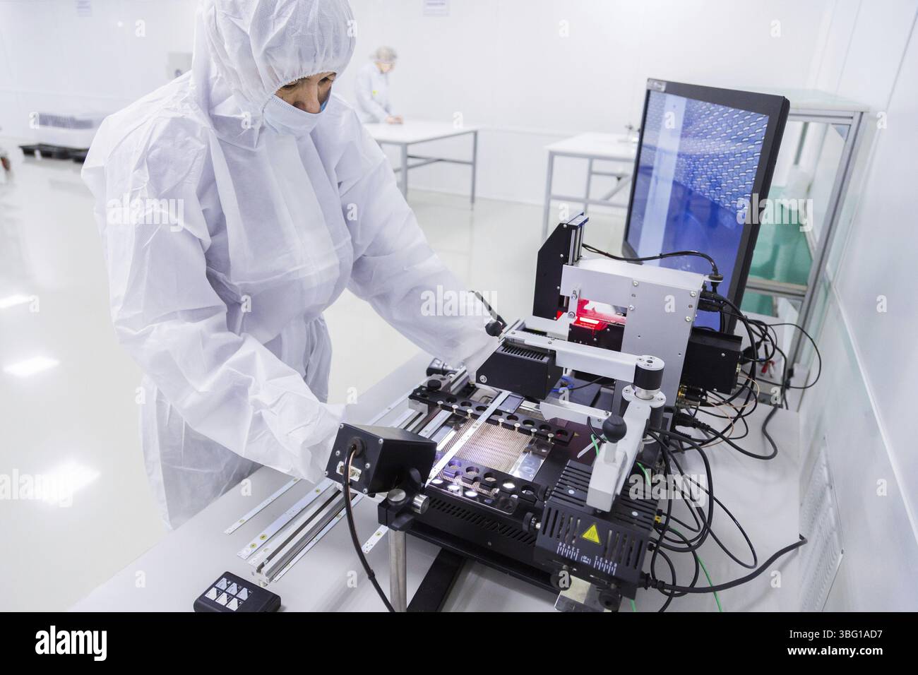 A factory worker in a white lab suit, latex gloves and face mask ...