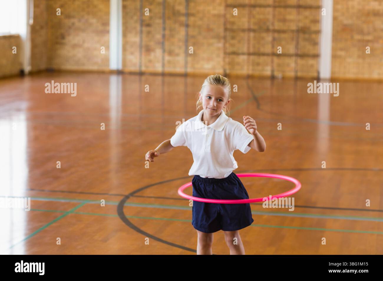 Girl spinning bright pink hula hoop in school gymnasium with colored ...