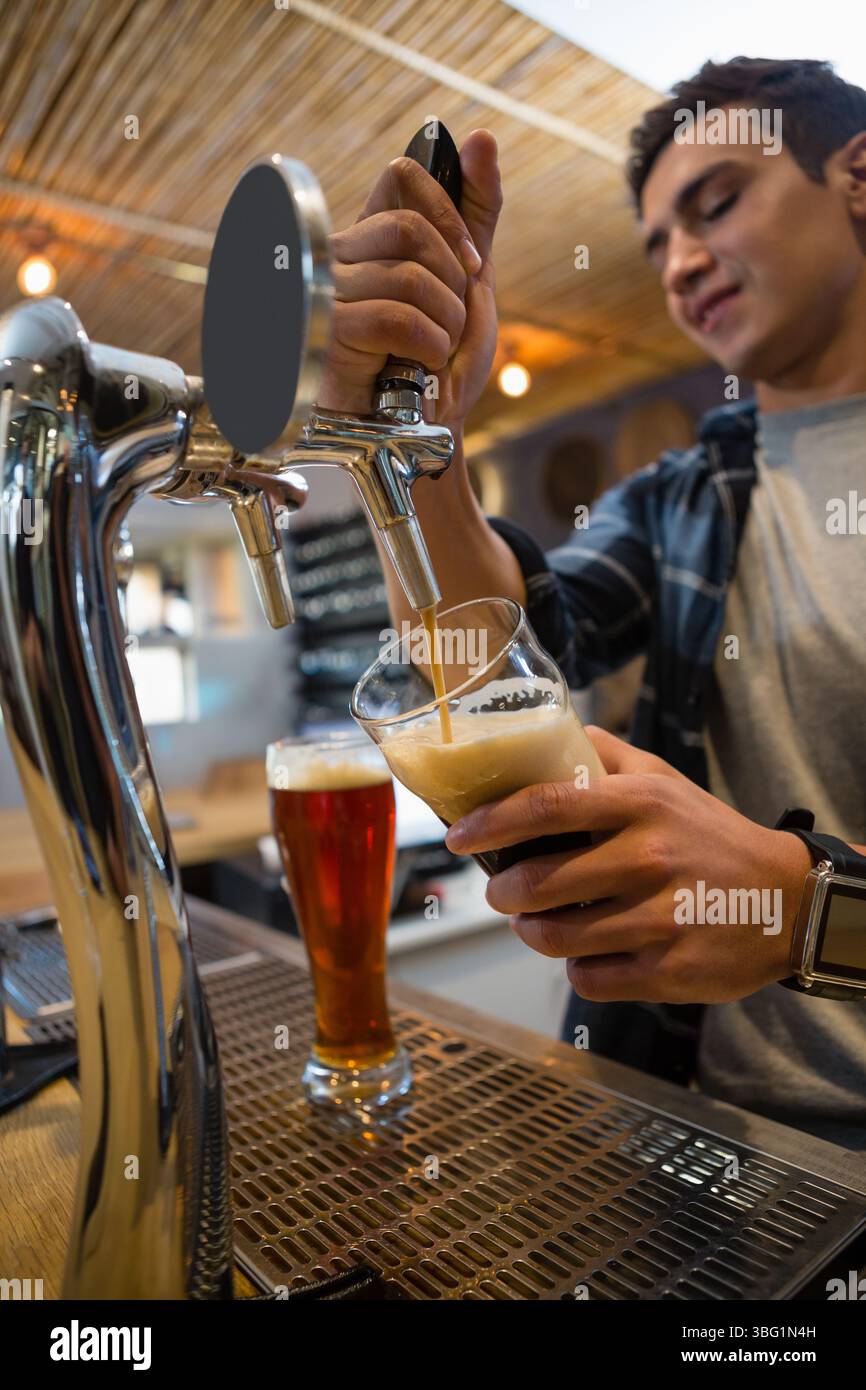Hispanic male bartender pouring amber beer from metal tap handle on bar ...