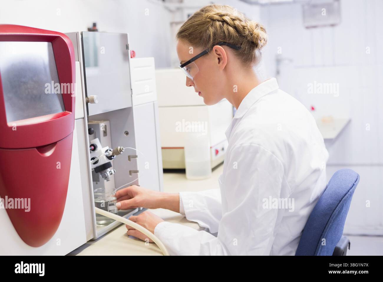 Analytical instrument processing samples at bright lab bench, with red housing and clear vials ...