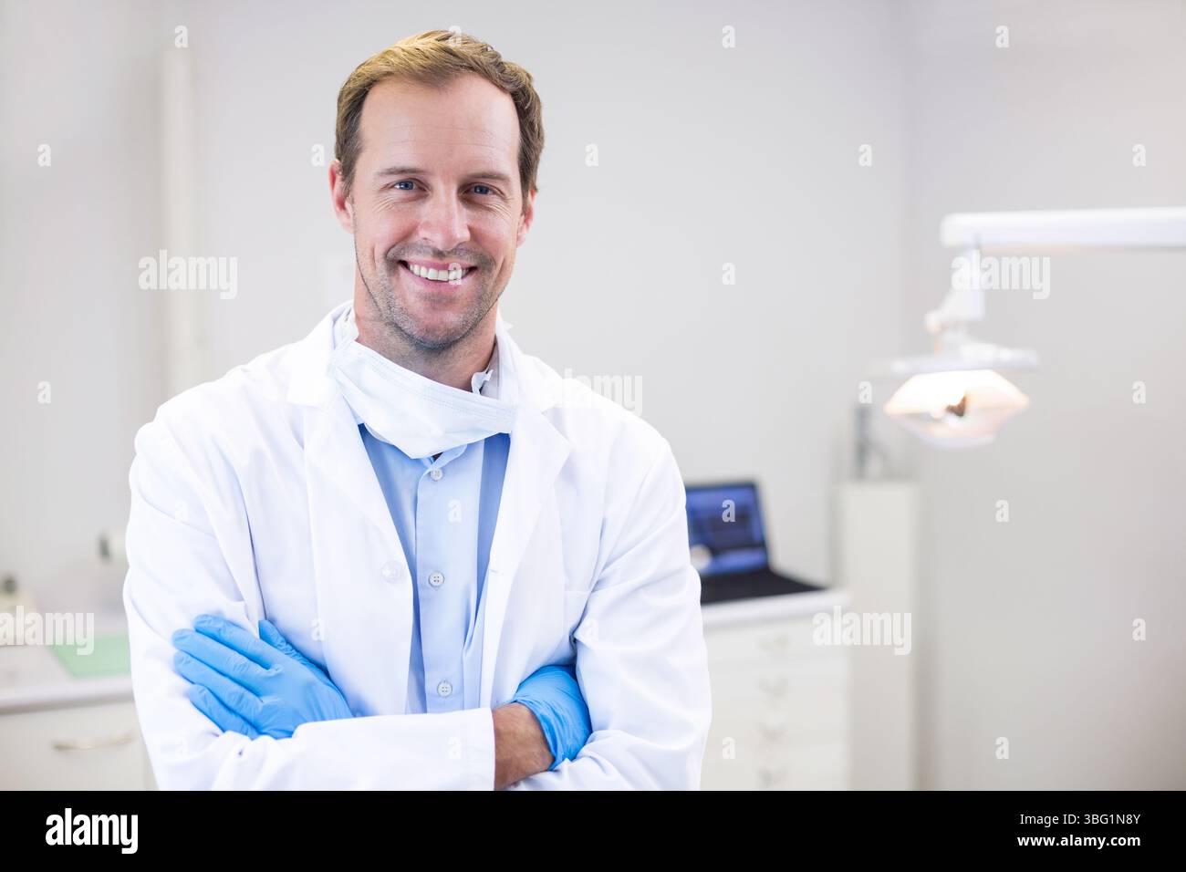Male dentist standing crossing arms in dental exam room showing exam ...