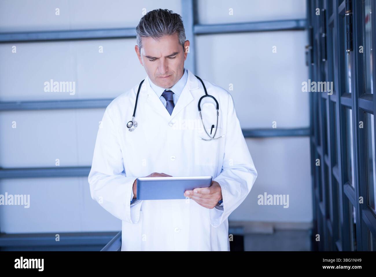 Male doctor wearing lab coat with stethoscope reviewing tablet in ...