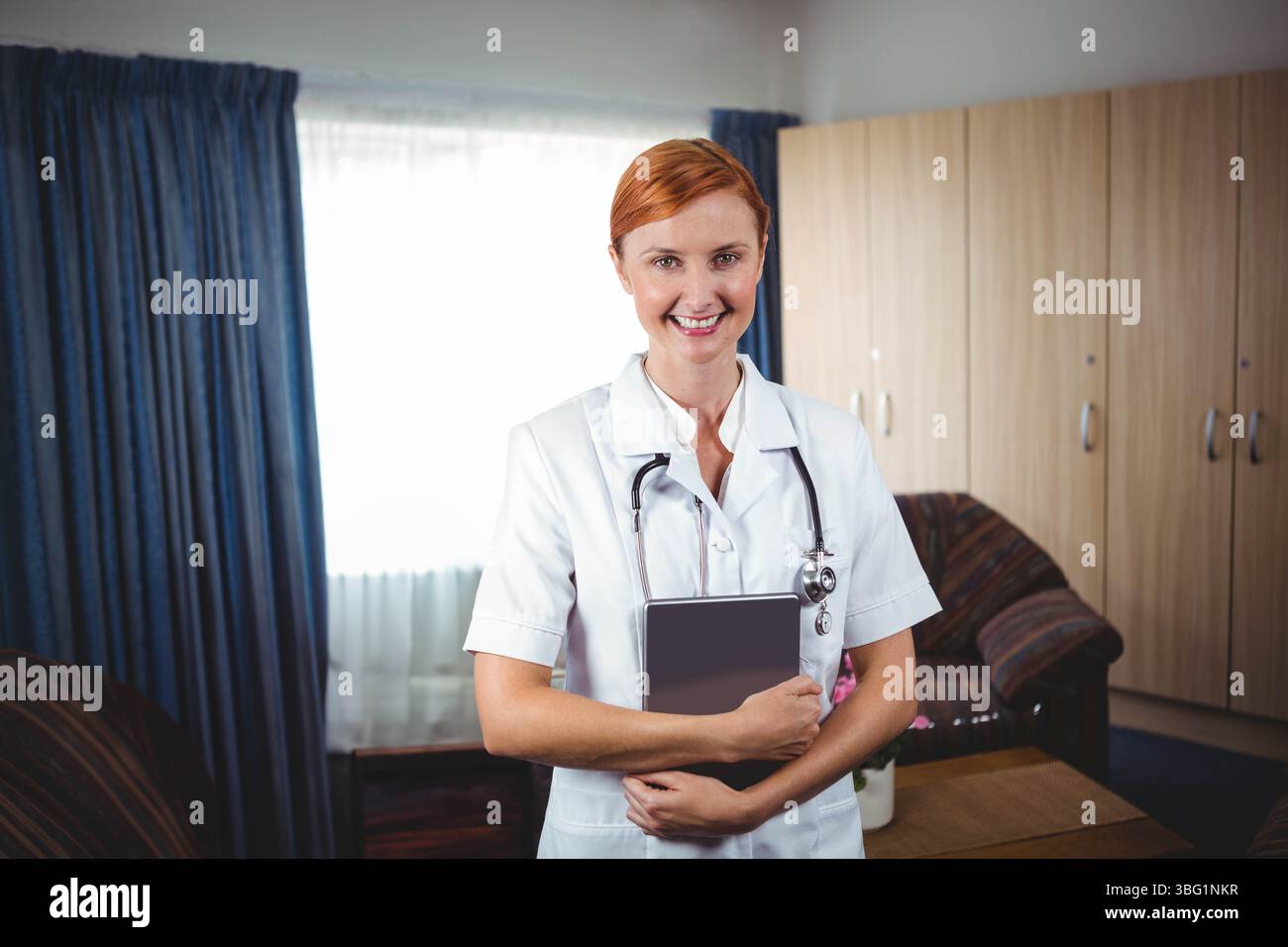 Female nurse standing in home care lounge holding tablet computer and ...