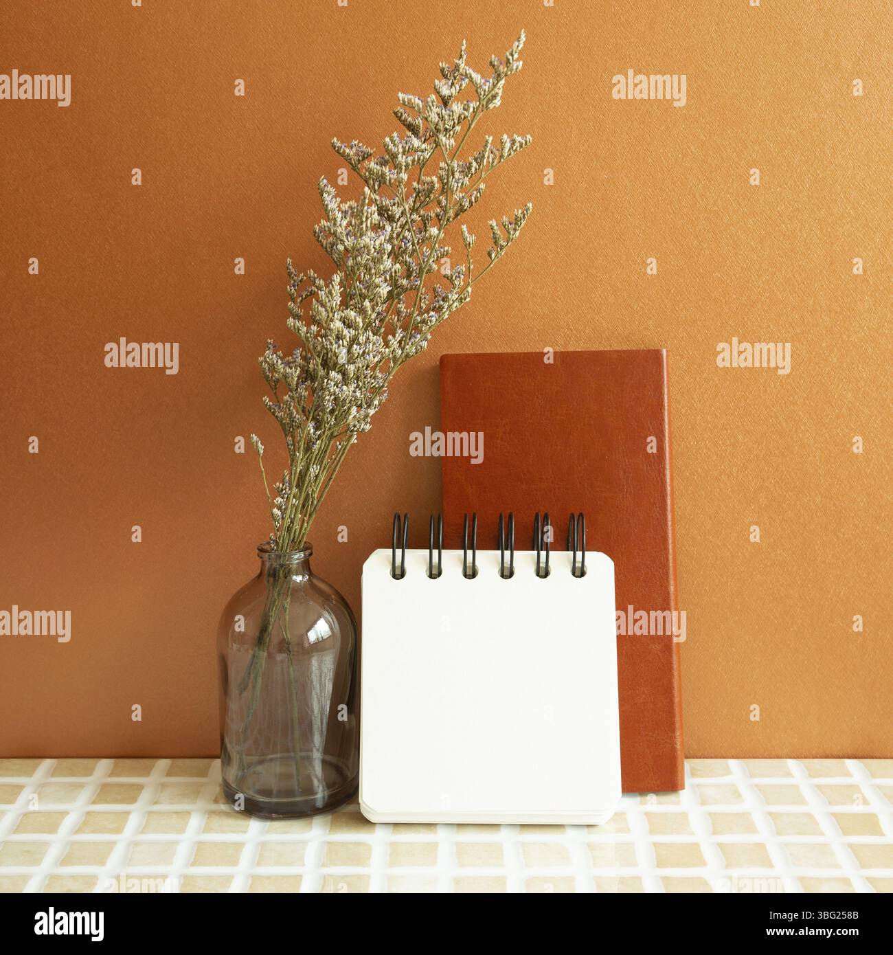 Notebooks and vase of misty blue dry flowers on beige ceramic mosaic ...