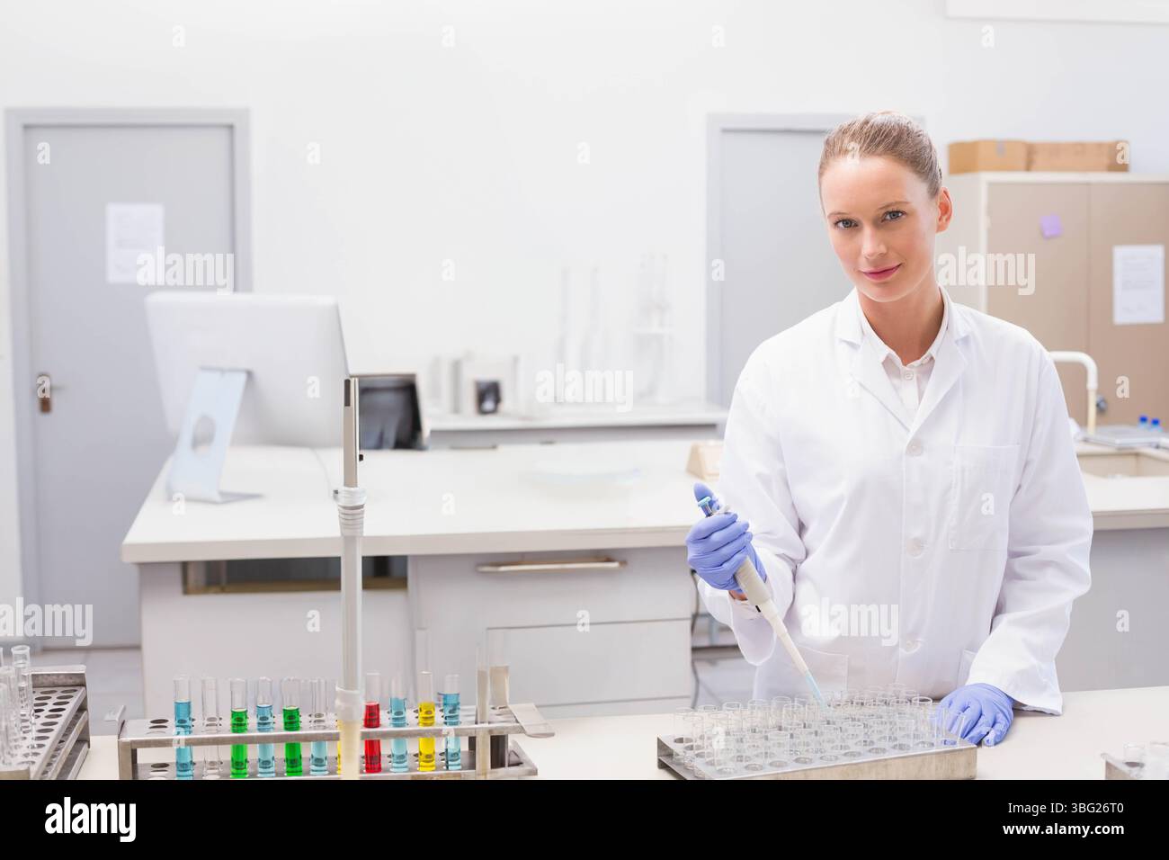 Female scientist wearing lab coat pipetting into multiwell plate at lab ...