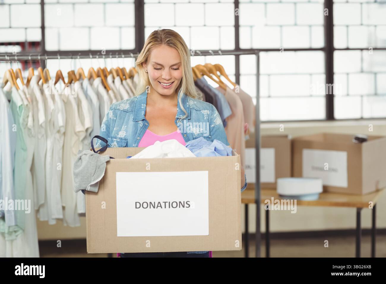 Female volunteer holding donation box sorting clothes in donation ...