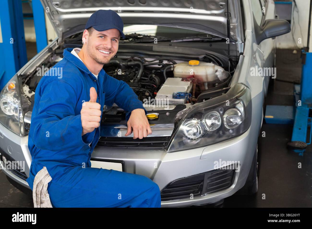 Adult male mechanic kneeling in workshop giving thumbs-up and raising ...