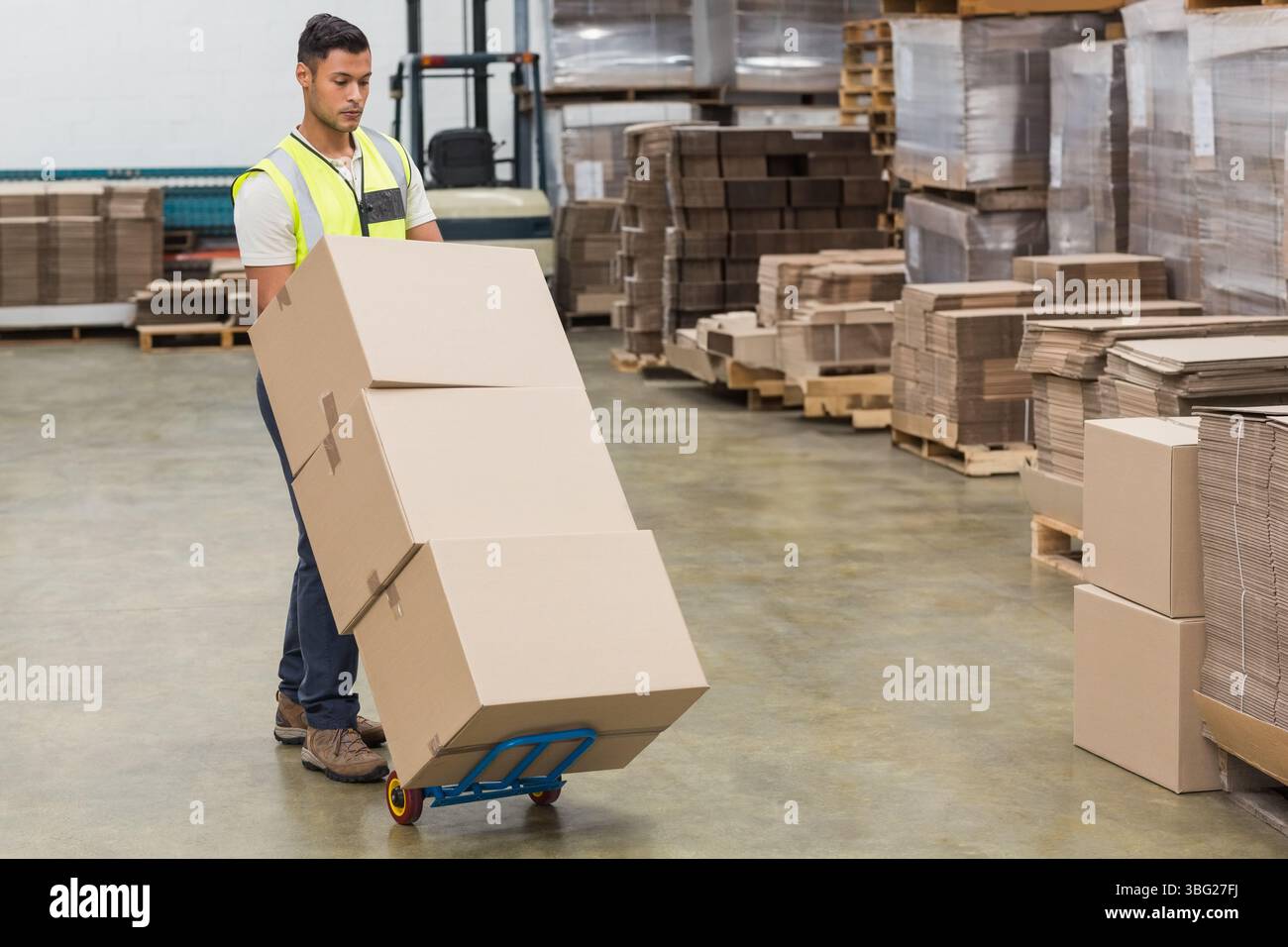 Hispanic male in safety vest pushing blue hand truck with cardboard ...