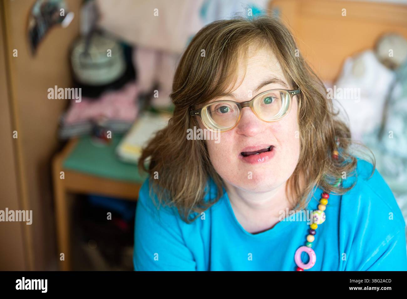 Portrait of a 42 yo happy woman with Down Syndrome in her sleeping room ...