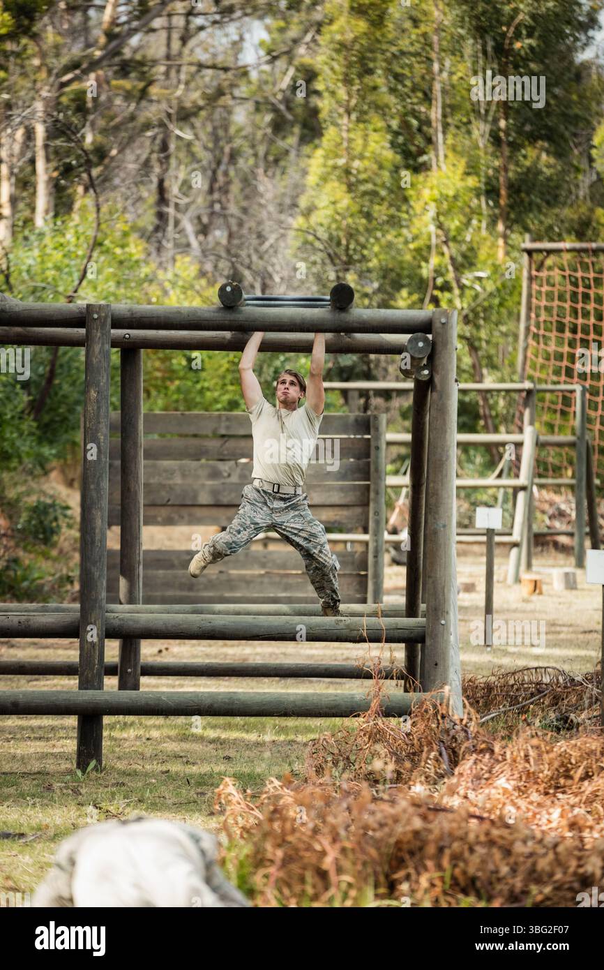 Male soldier swinging from log above beams in forest obstacle course ...