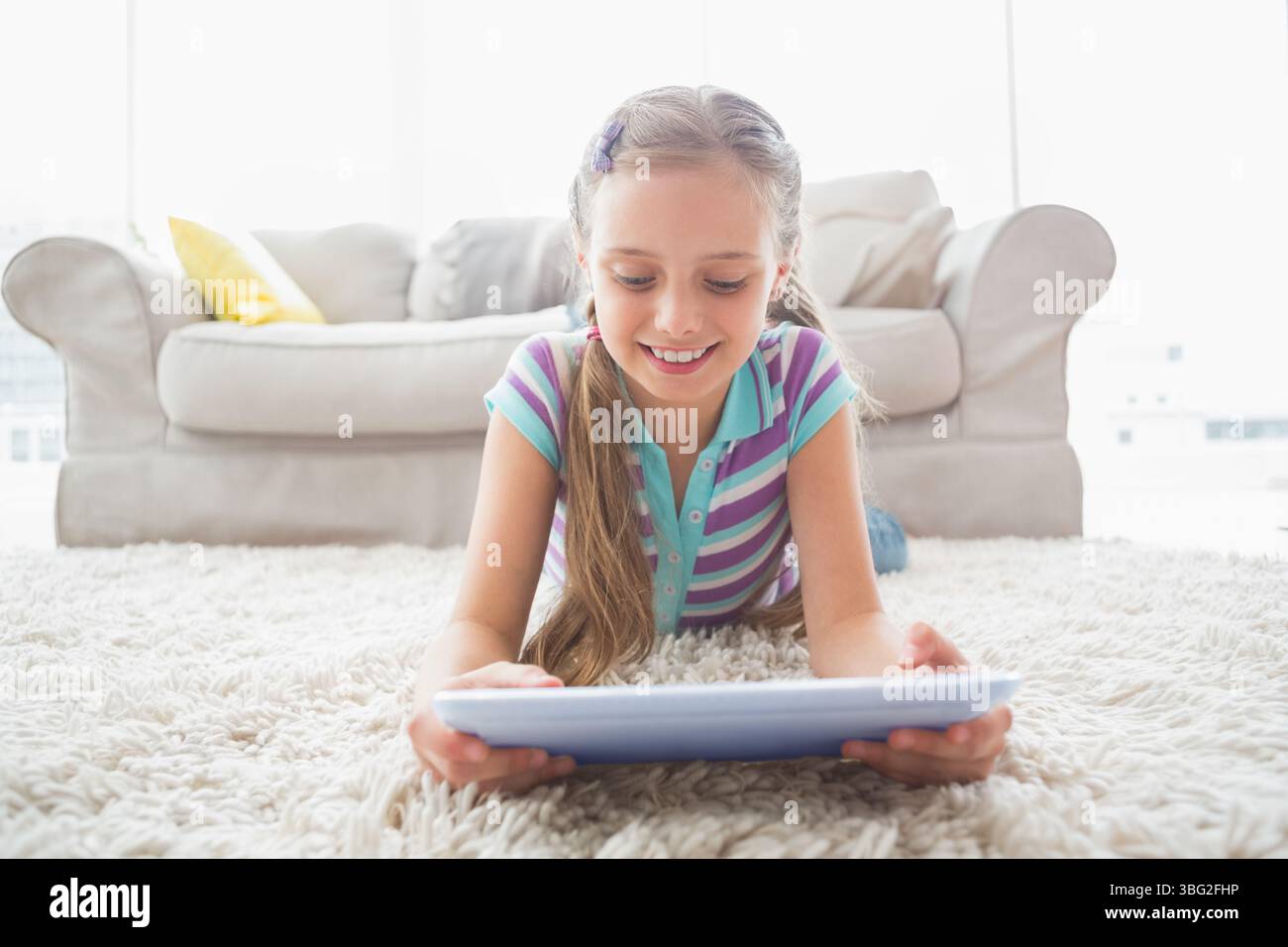 School-aged girl lying on plush rug under windows at home holding ...