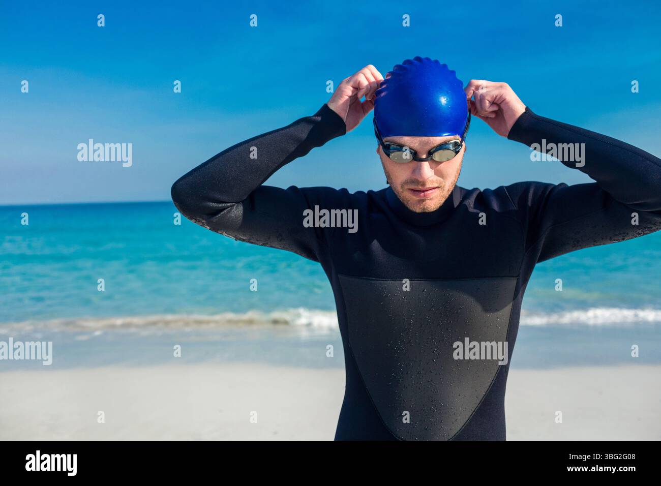 Male swimmer adjusting cap and wearing black wetsuit with goggles on ...