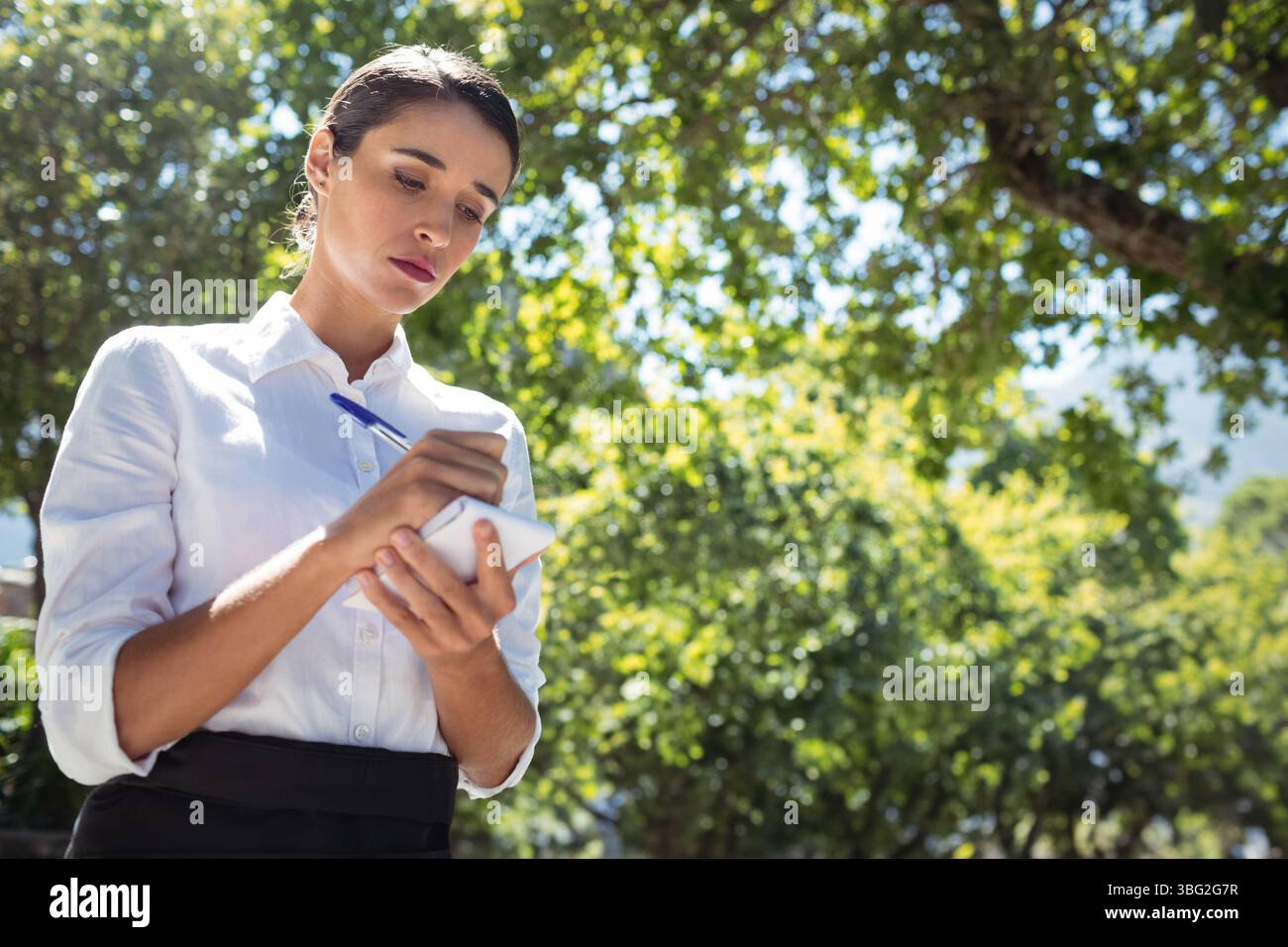 Late twenties woman standing under park trees in business attire ...