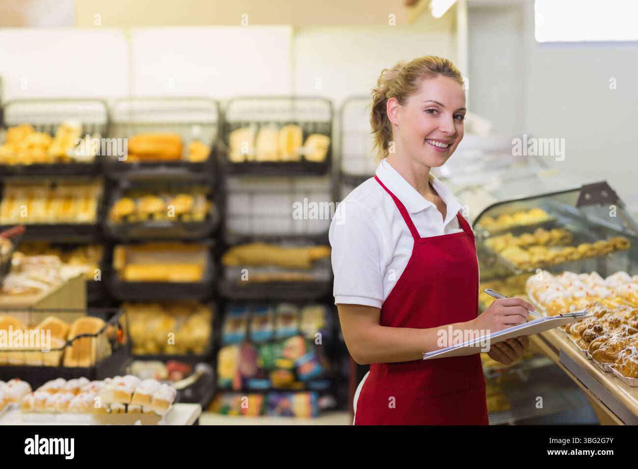 Female bakery worker holding clipboard inspecting bread racks and ...