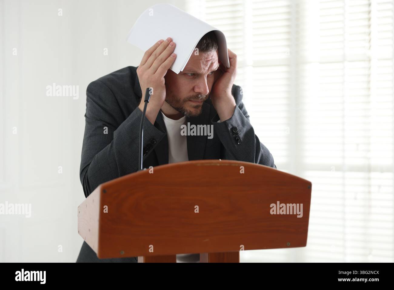 Fear of public speaking. Nervous man with microphone at lectern indoors ...