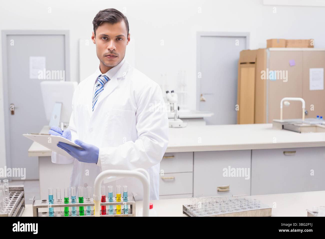 Male scientist recording on clipboard at lab bench near test tubes and ...