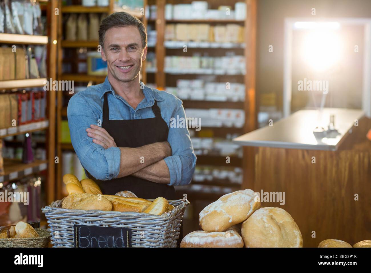 Male shopkeeper wearing apron standing behind basket of baguettes and ...