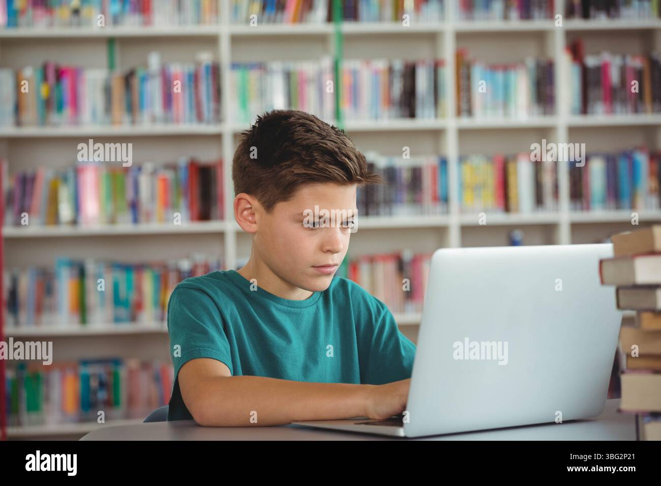Male child studying on silver laptop at table in school library reading ...