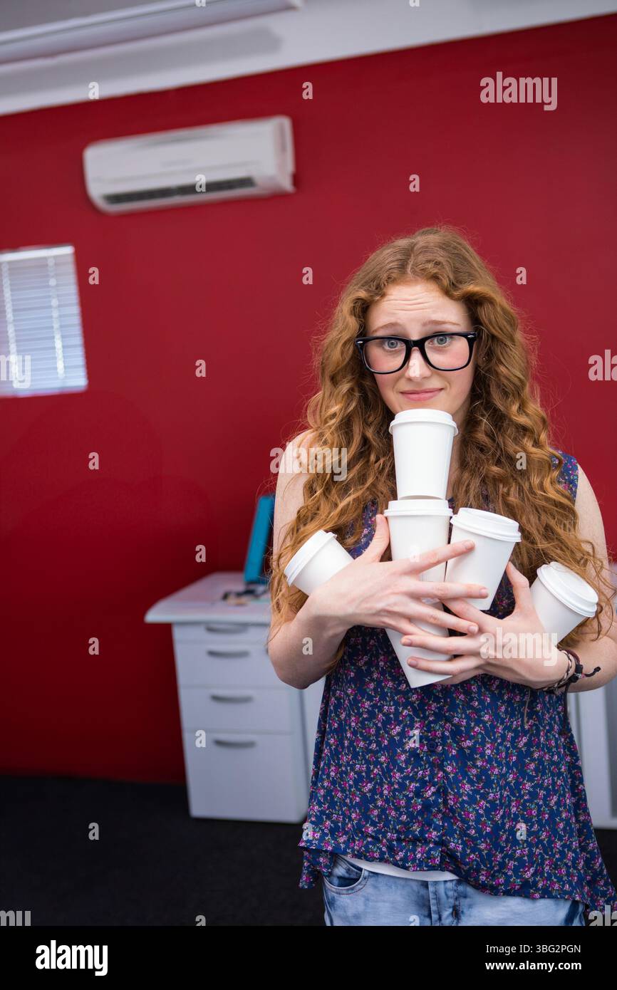 Female office worker holding disposable coffee cups against chest in ...