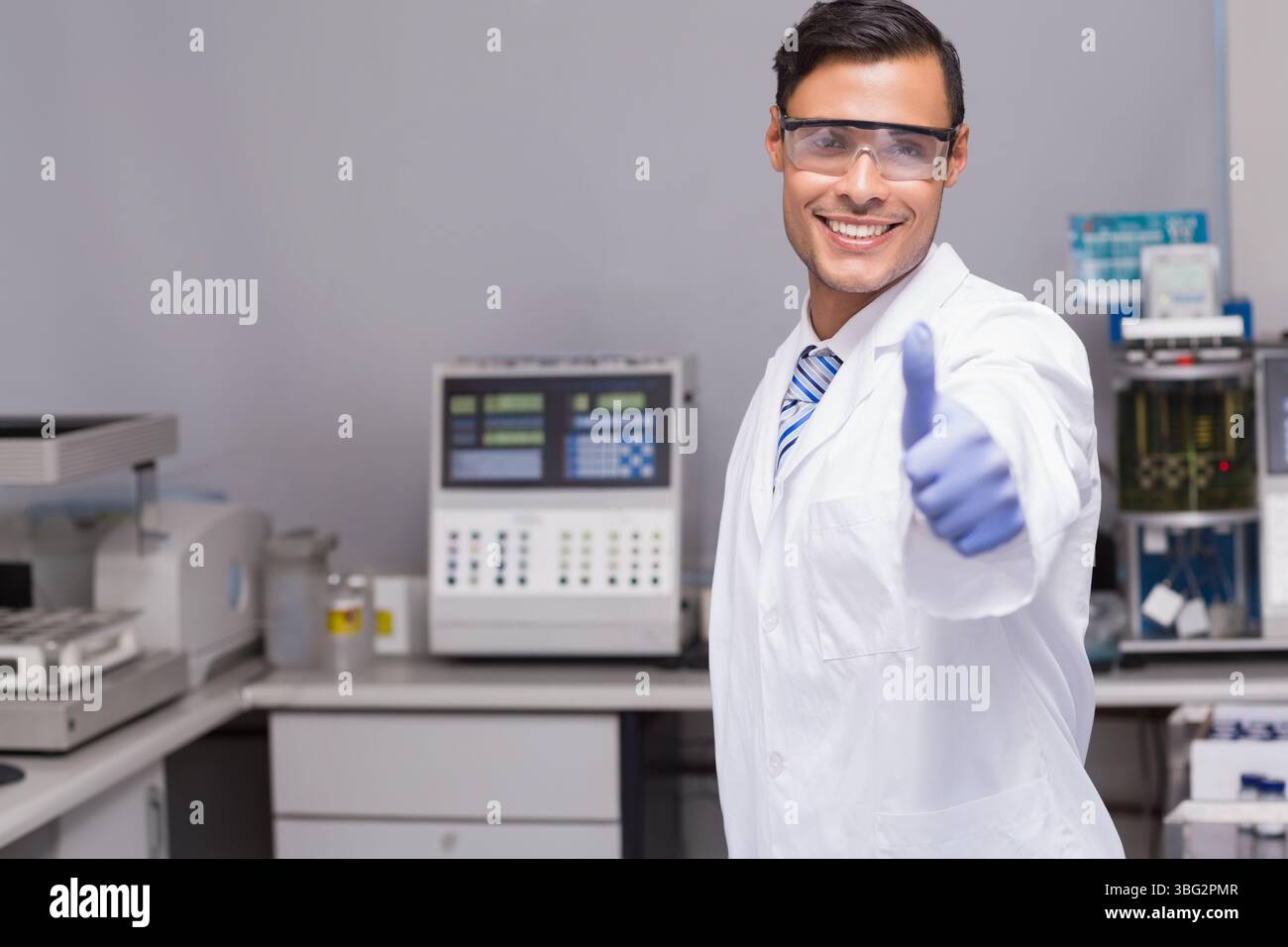 Male lab tech wearing lab coat operating analyzers in clinical lab with reagent bottles, copy ...