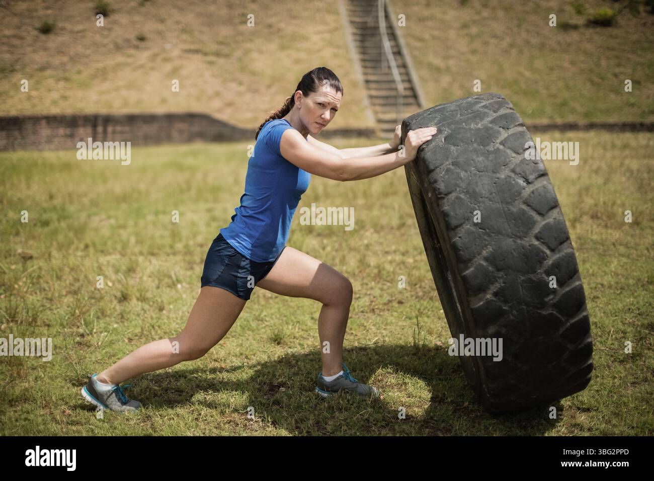 Female athlete in sportswear pushing tractor tire on grassy field by ...