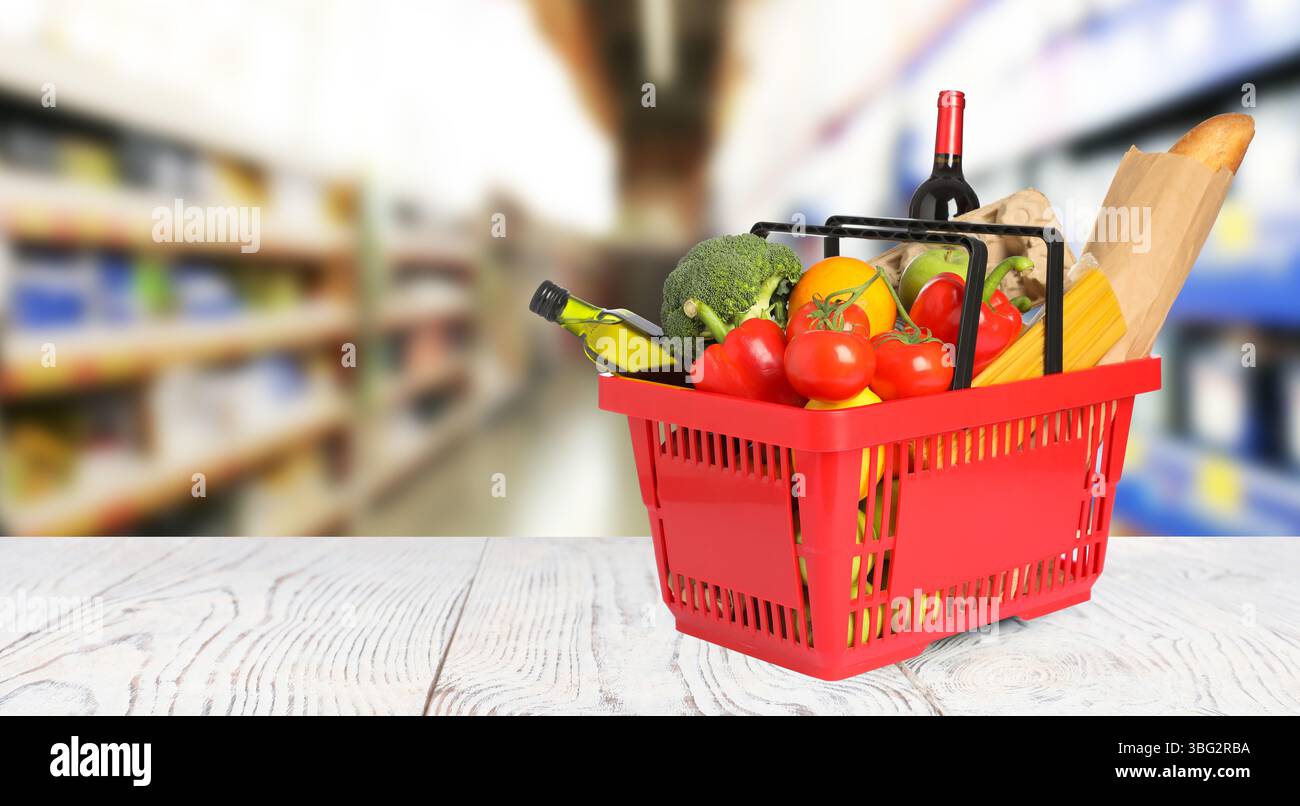 Red shopping basket full of groceries on wooden table in supermarket ...
