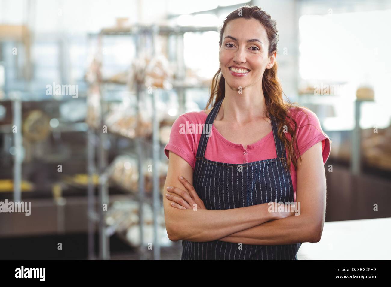 Female baker standing behind counter in bakery wearing striped apron ...