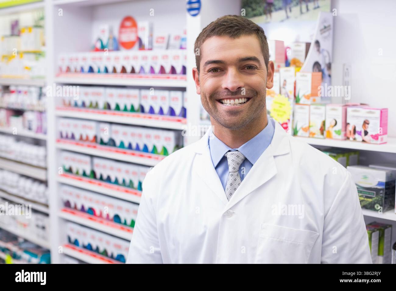 Male pharmacist standing in pharmacy aisle with medicine boxes wearing ...