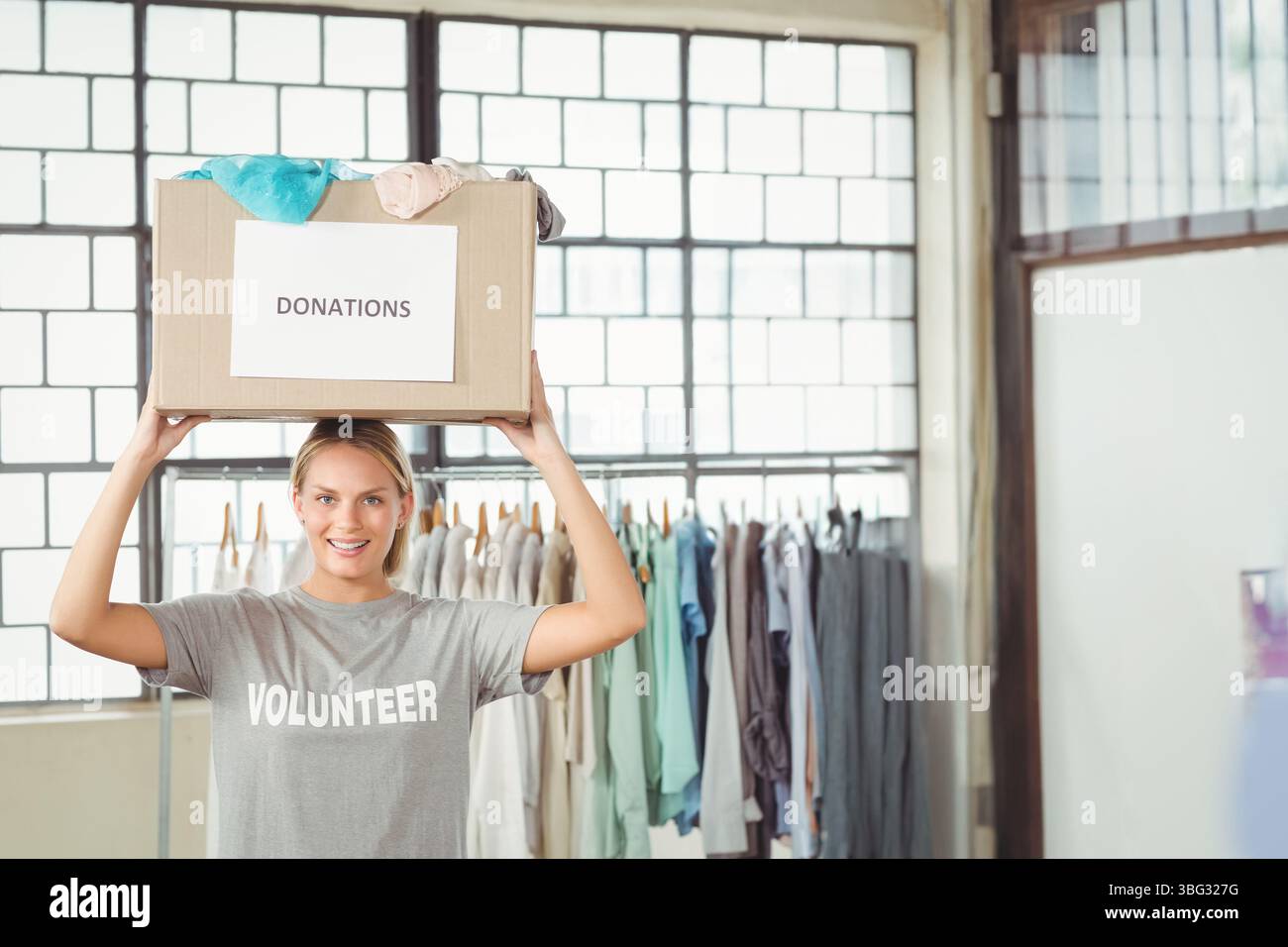 Female volunteer balancing Donations box on head while sorting garments ...