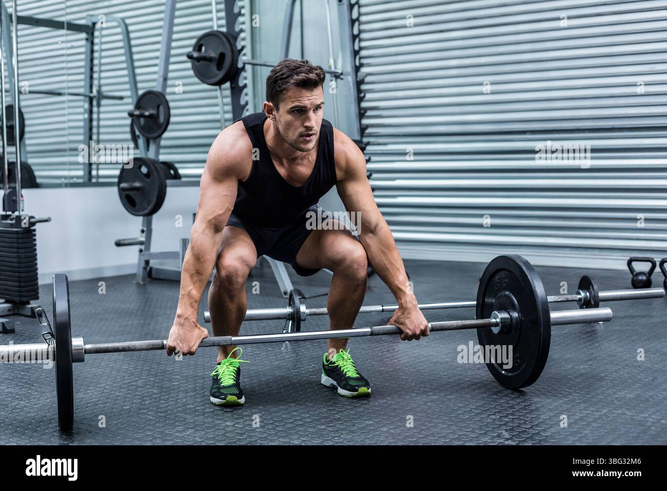Athletic man squatting with loaded barbell at gym wearing black shoes ...