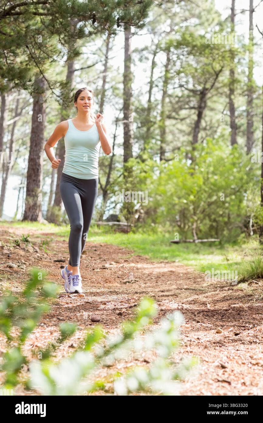 Woman in late twenties jogging on dirt trail through pine forest ...
