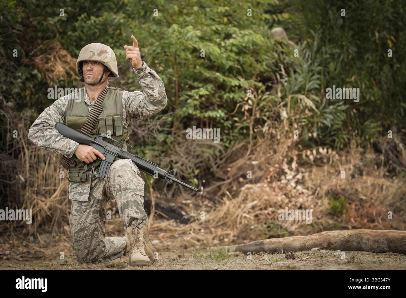 Adult male soldier kneeling on one knee in forest edge holding assault ...