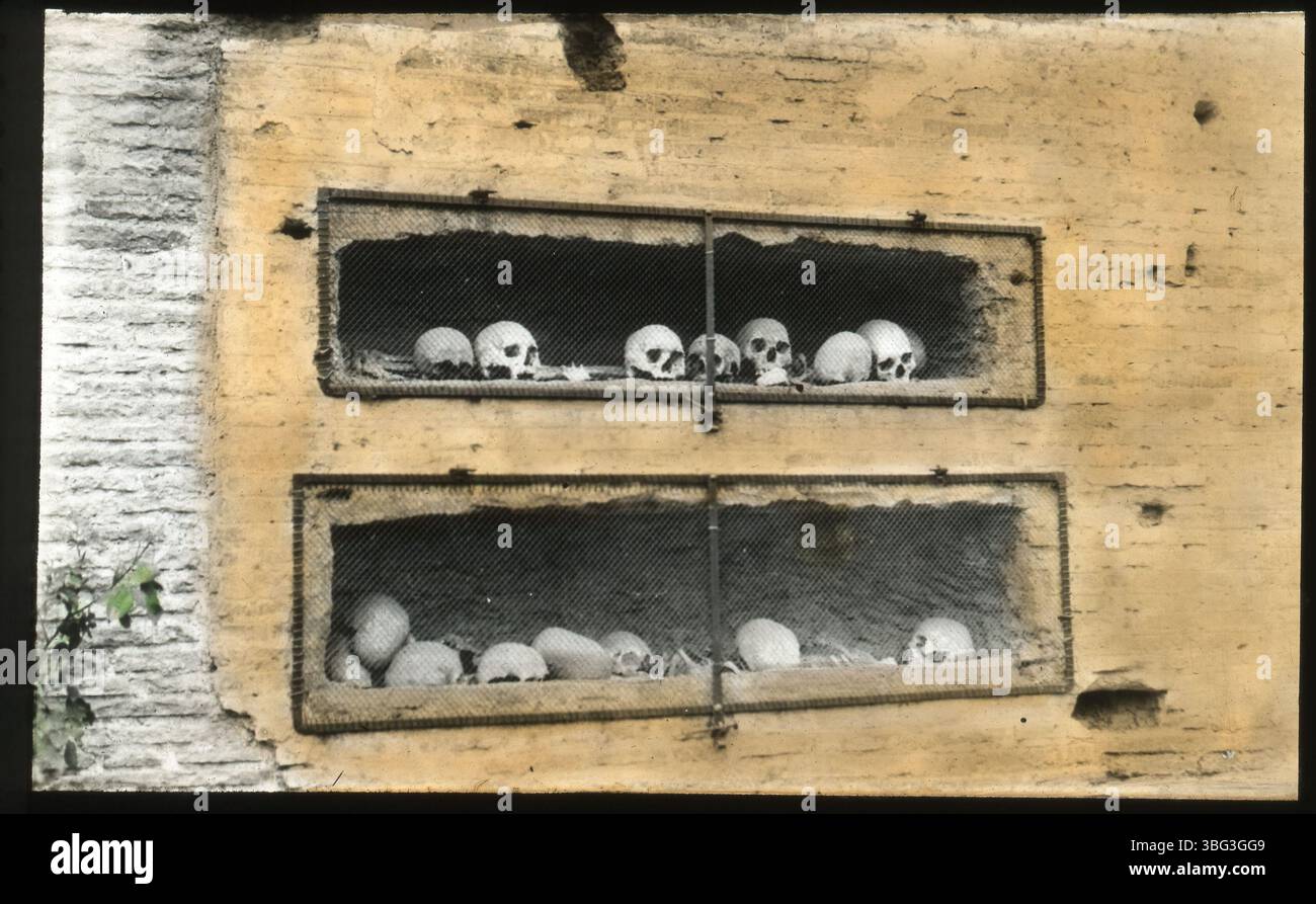 This 1913 photograph shows rows of skulls in wall niches behind wire ...