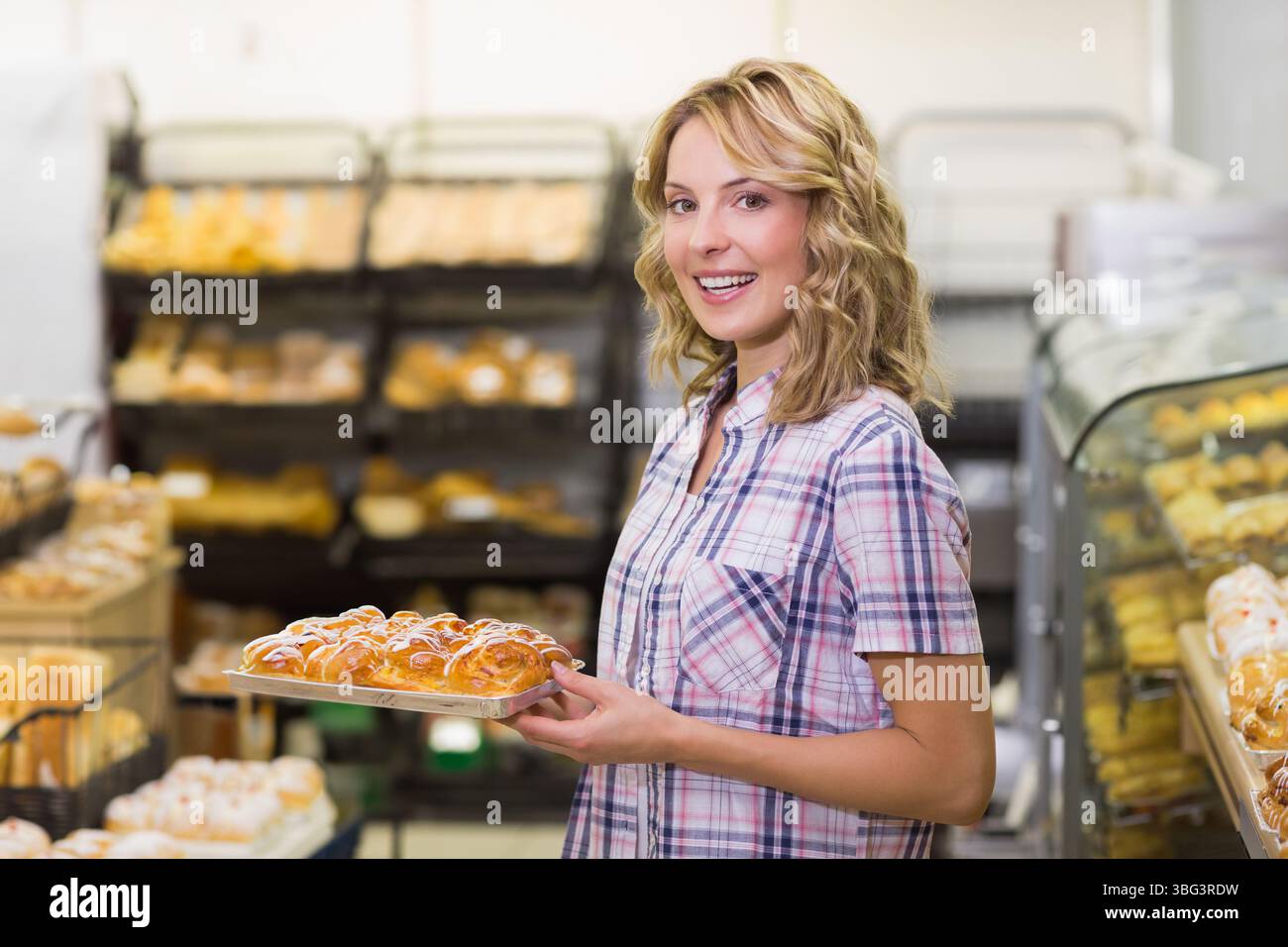 Female bakery clerk wearing plaid shirt presenting tray of braided buns ...