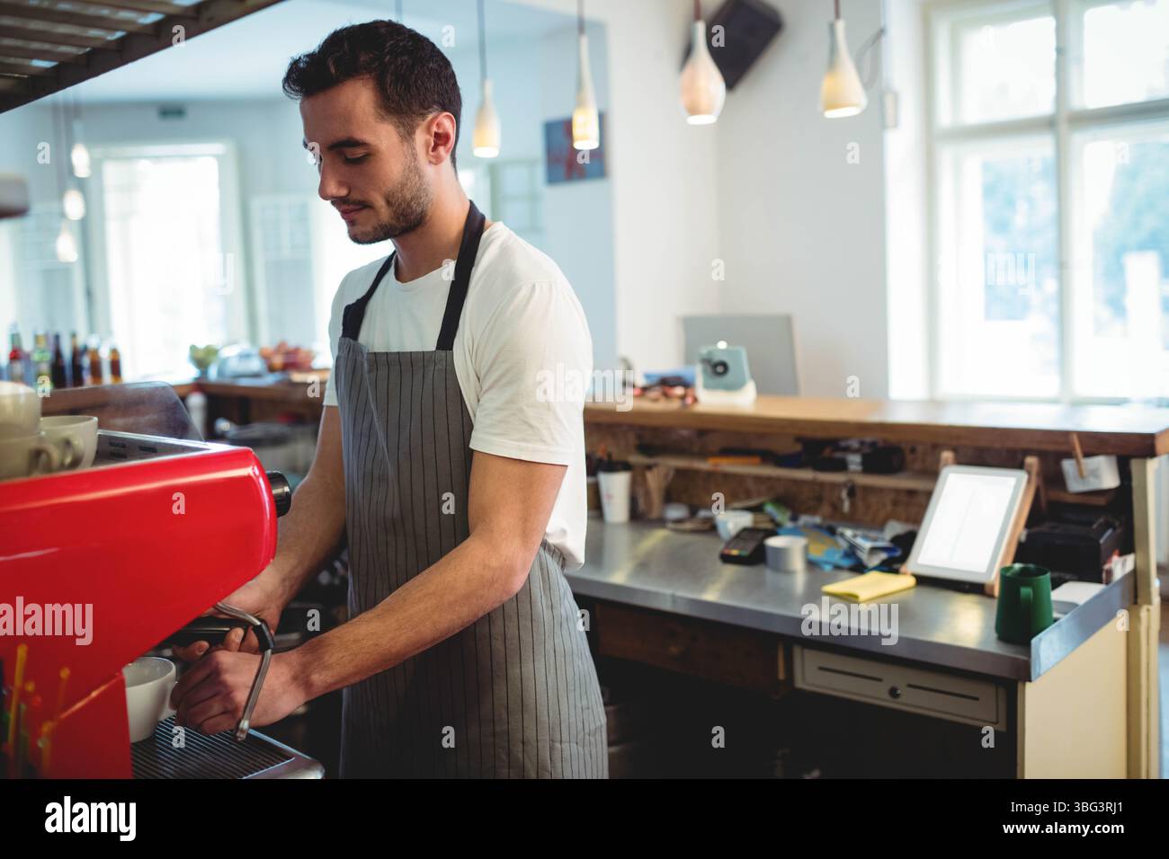 Male barista operating red espresso machine behind wooden counter in ...