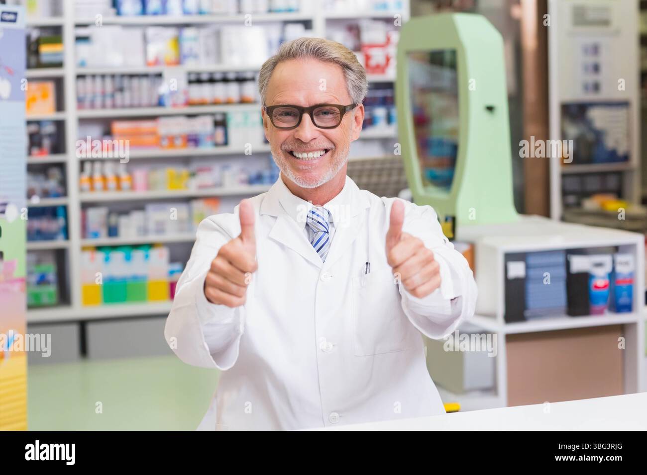 Senior male pharmacist wearing lab coat giving thumbs up behind counter ...