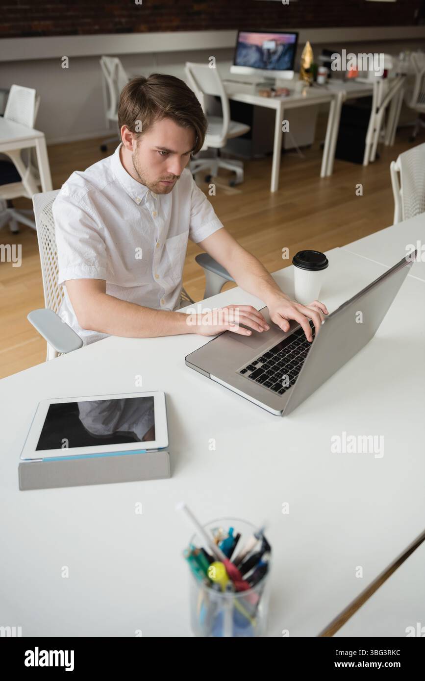 Man wearing short-sleeve shirt typing on laptop at office desk with ...