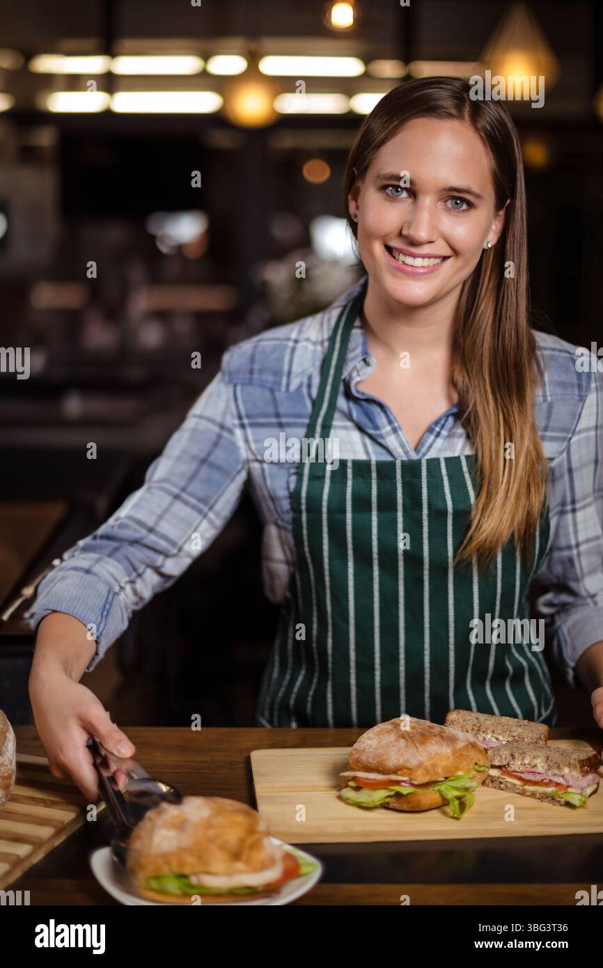 Female barista standing behind wooden counter assembling sandwiches in ...