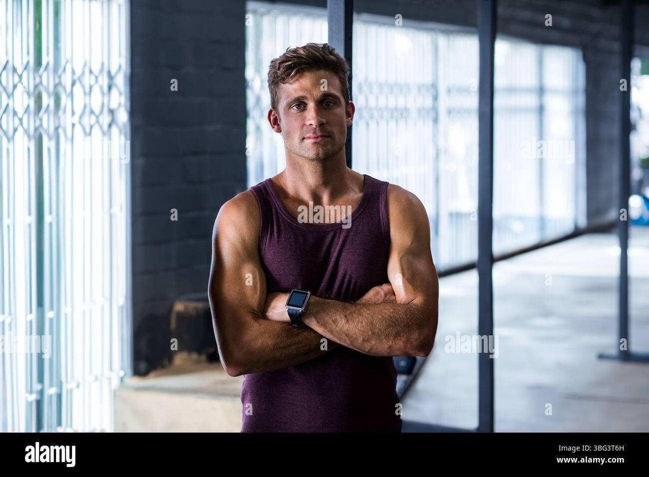 Muscular man standing with arms crossed in gym wearing smartwatch near ...
